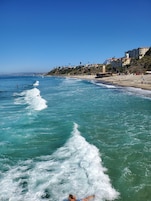 Uma praia com ondas, areal e edifícios ao fundo.