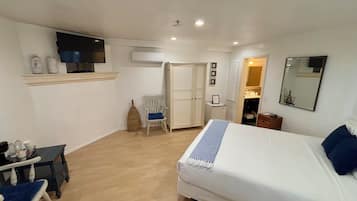 Quarto com cama, uma cadeira, escrivaninha e televisão.