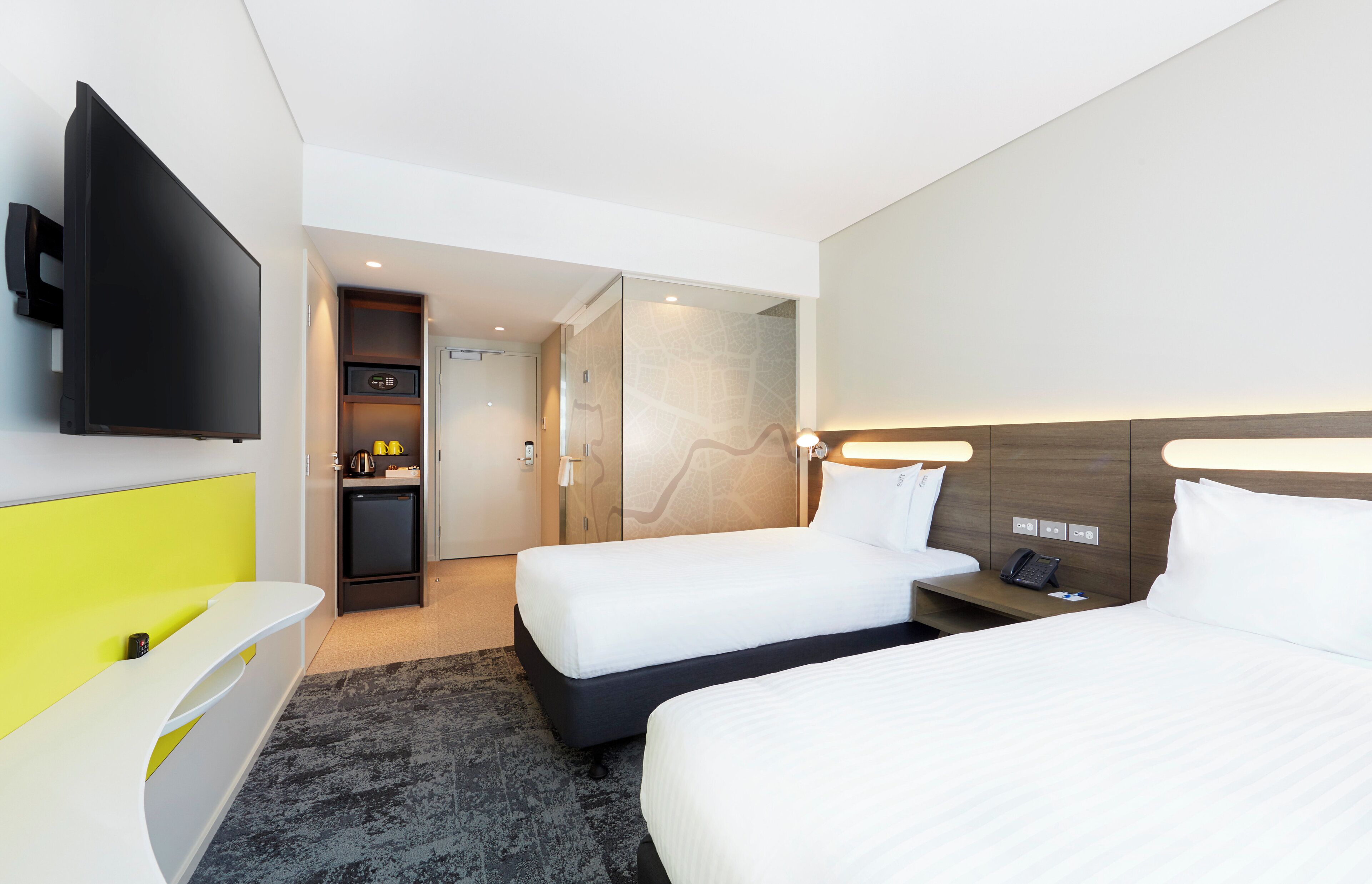Quarto de hotel com duas camas, uma escrivaninha, televisão de tela plana, minibar e banheiro com chuveiro e vaso sanitário.