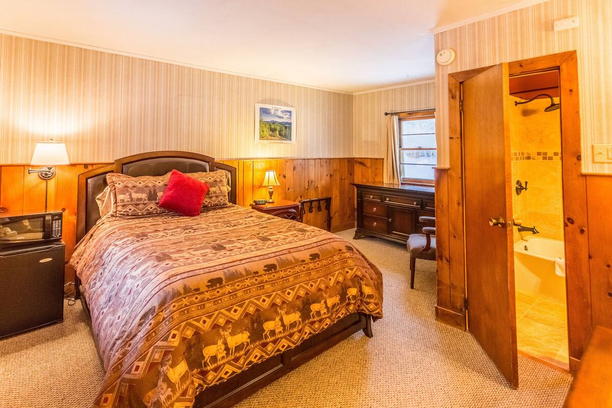 Quarto com cama, mesas de cabeceira, escrivaninha e porta para um banheiro.