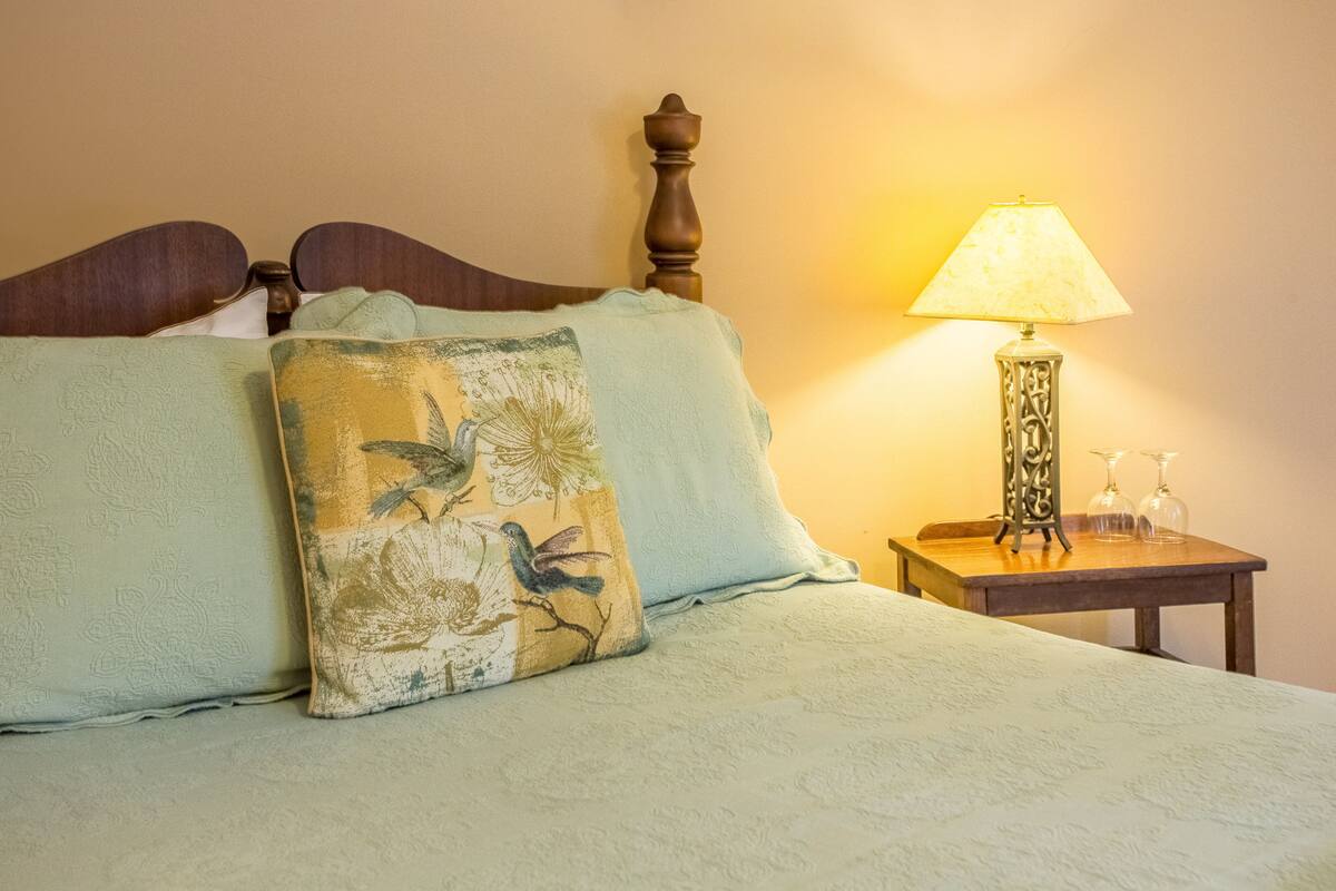 Uma cama bem arrumada com almofada estampada e uma luminária em um criado-mudo de madeira.