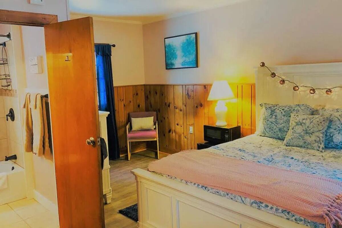 Quarto com cabeceira de madeira, cama com roupa de cama floral, abajur e uma cadeira.
