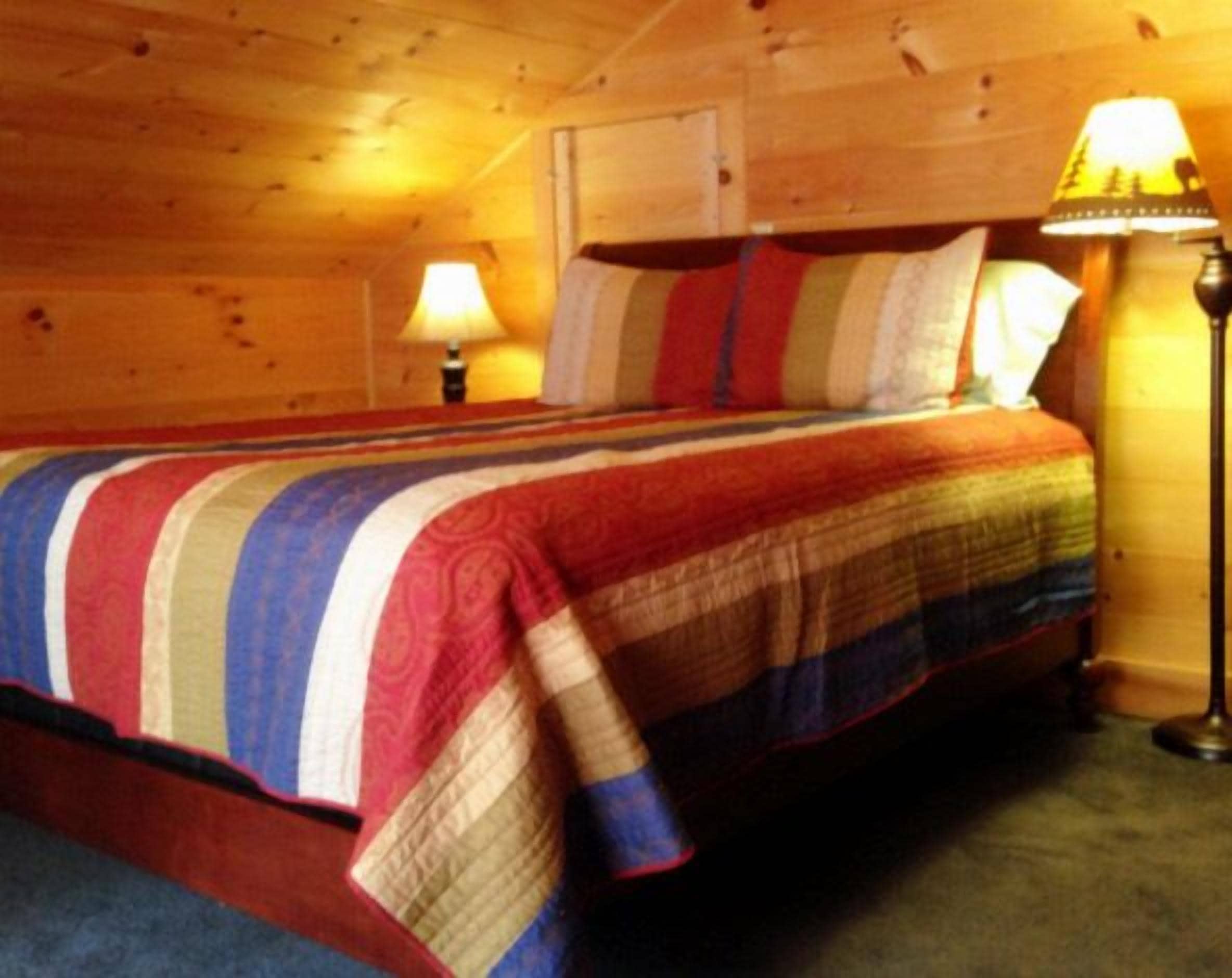Quarto de cabana de madeira com uma cama, duas luminárias e uma janela.