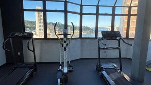 Uma academia com duas esteiras e um elíptico, grandes janelas com vista para a cidade.