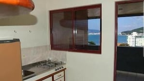 Uma cozinha com fogão a gás, janela com vista para o mar e varanda com vista para edifícios.