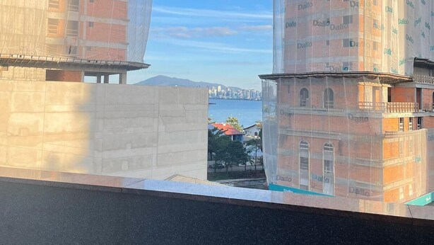 Vista de dentro de um edifício, mostrando uma área de construção com andaimes e o horizonte da cidade ao fundo.