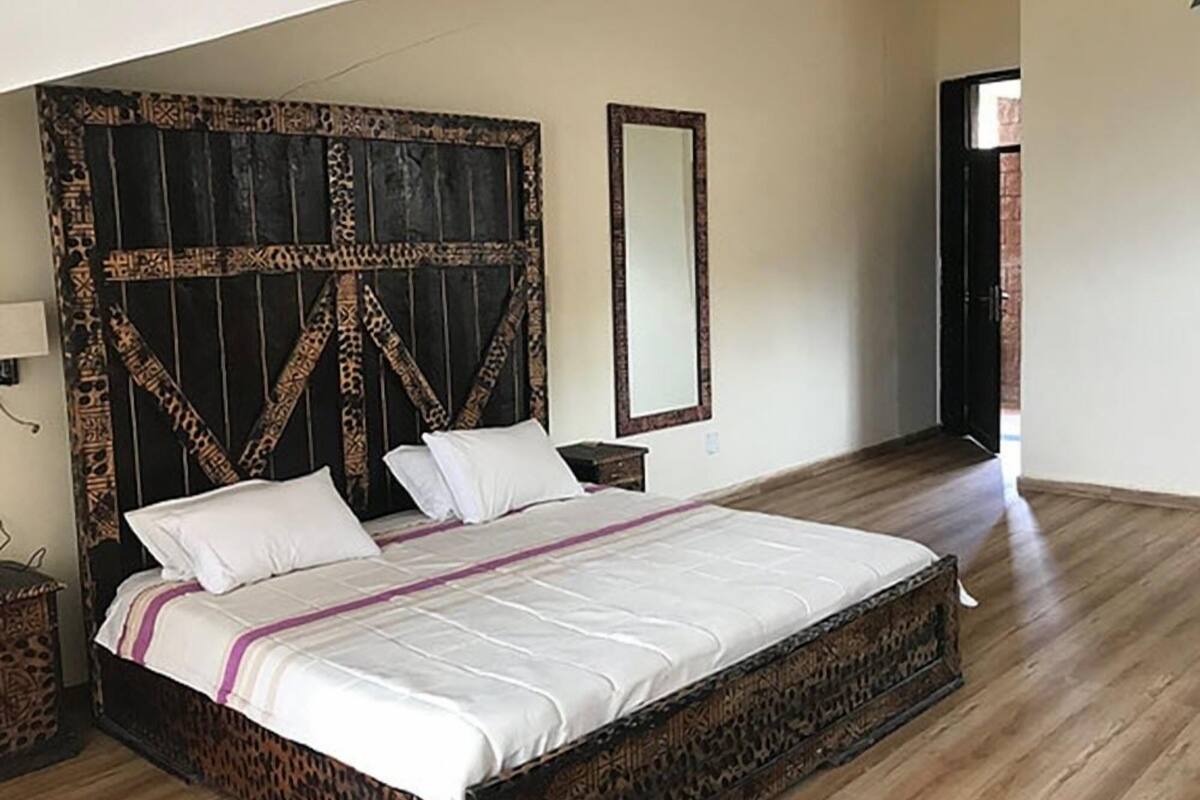 Quarto com uma cama grande, cabeceira de madeira com padrão geométrico, mesa de cabeceira e um espelho na parede.