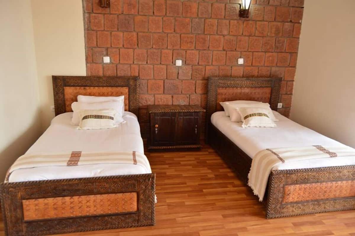 Quarto com duas camas de madeira, uma parede de tijolos e um pequeno armário de madeira.