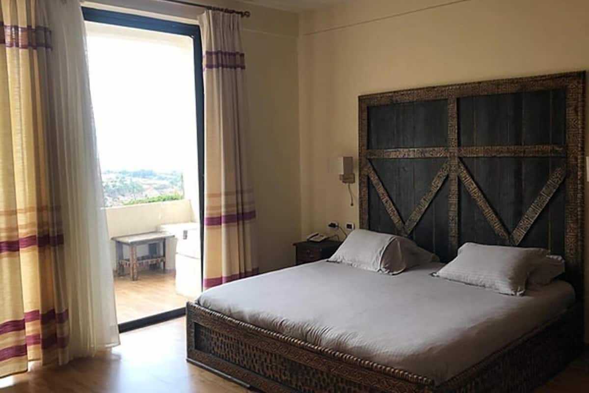 Quarto com cama grande, cabeceira de madeira e vista para área externa por uma porta de correr.