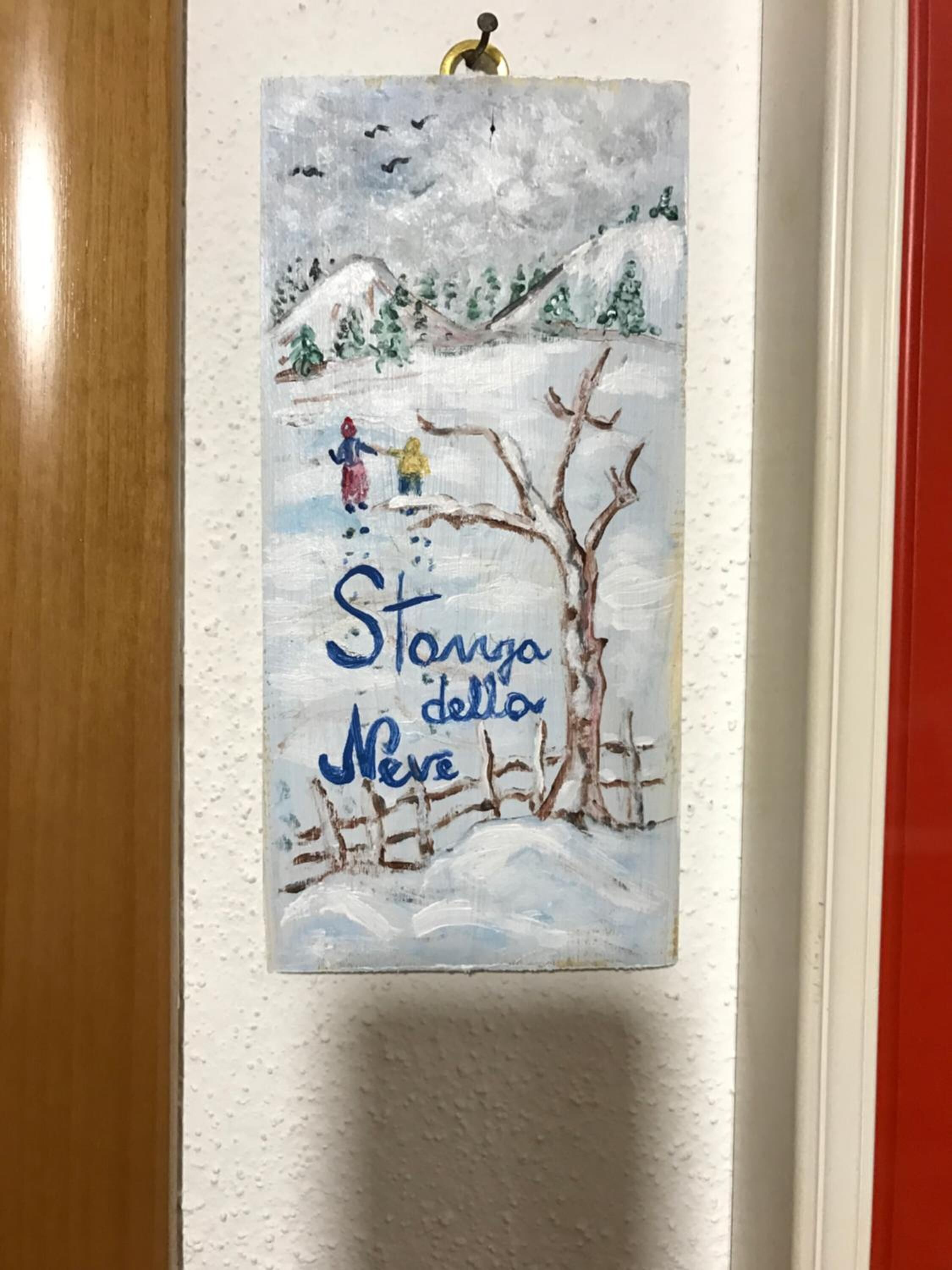 Obra de arte pendurada na parede retratando uma paisagem nevada com duas crianças e um cachorro, e o texto 'Stanga della Neve'.
