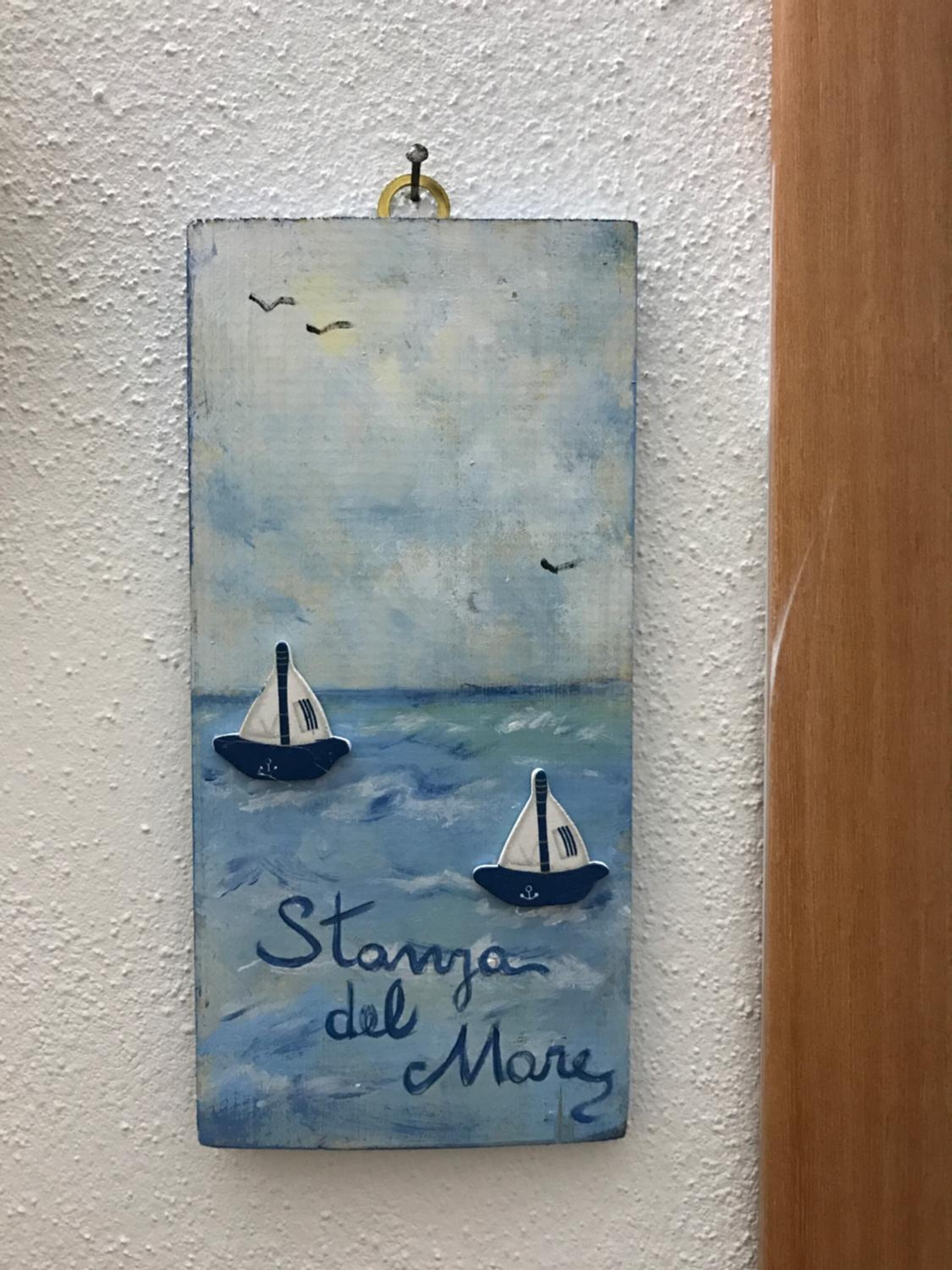 Obra de arte pendurada na parede retratando dois veleiros em um mar azul, com o texto 'Stanga del Mare'.