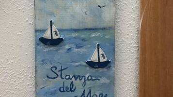 Obra de arte pendurada na parede retratando dois veleiros em um mar azul, com o texto 'Stanga del Mare'.