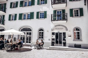 Um edifício com várias janelas, um letreiro com a inscrição 'River Residence' e área externa com mesas e cadeiras.