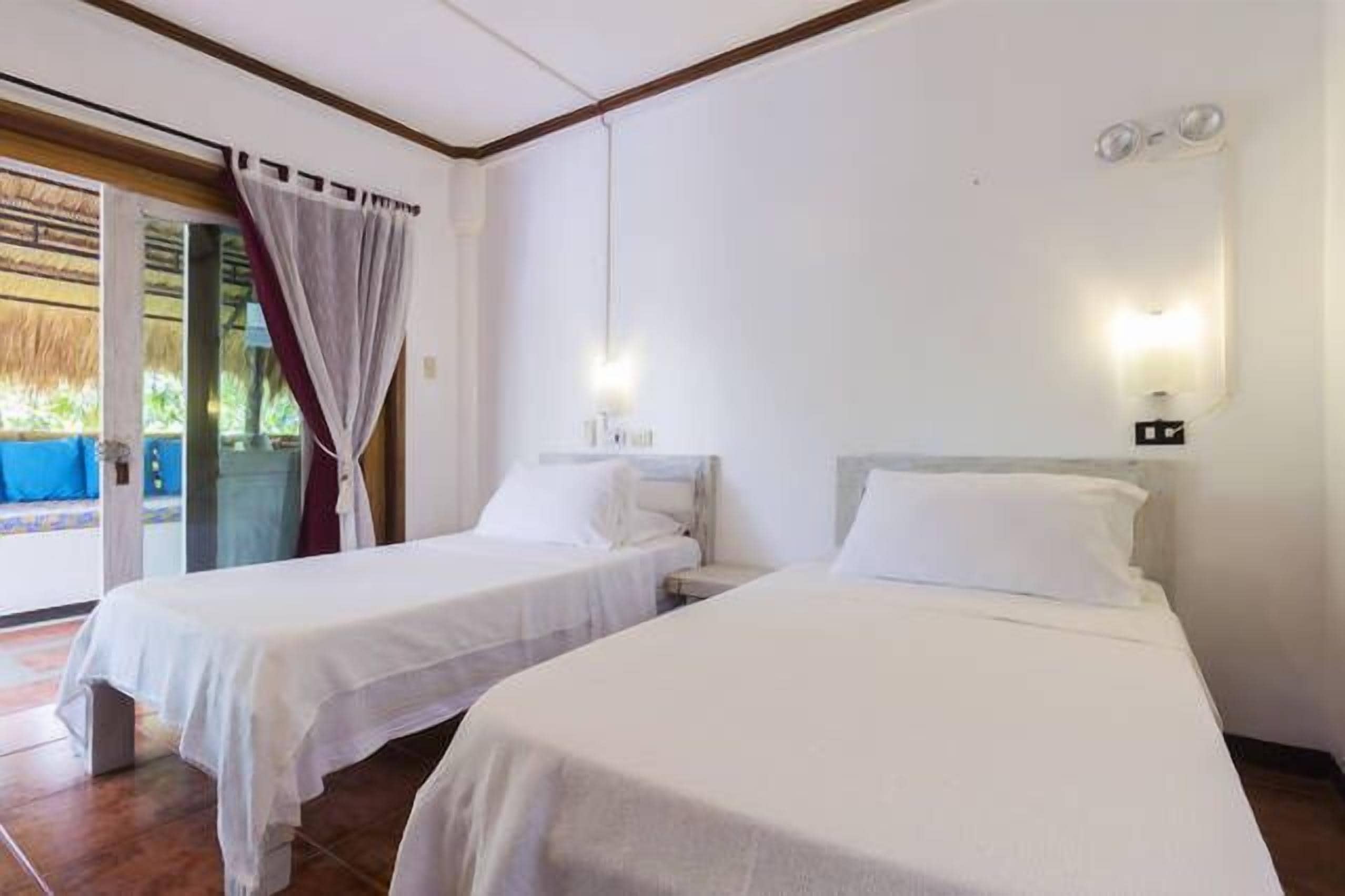 Quarto de hotel com duas camas de solteiro, uma porta de vidro deslizante que dá para uma área externa e uma luminária fixada na parede.