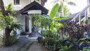 Um jardim tropical com uma estrutura de telhado de palha, rodeado por diversas plantas e árvores.