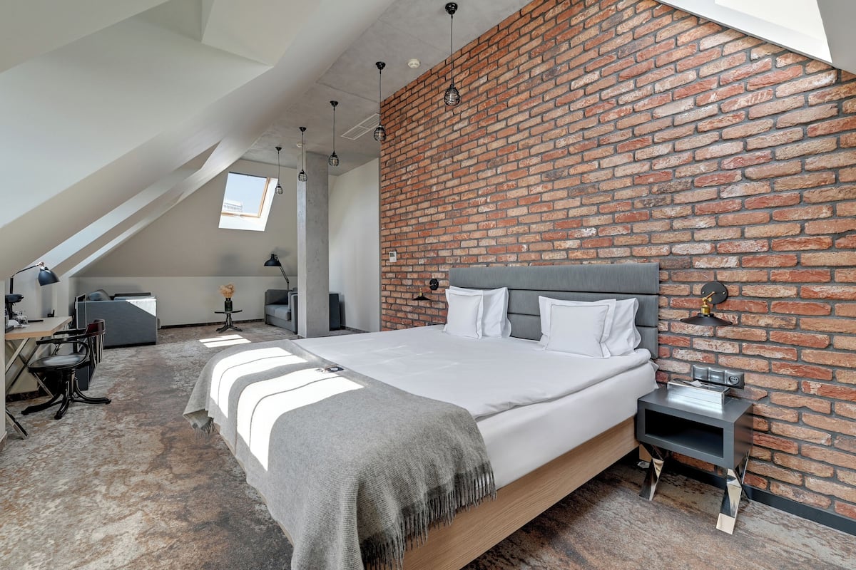 Quarto com parede de tijolos, uma cama, uma escrivaninha e uma cadeira.
