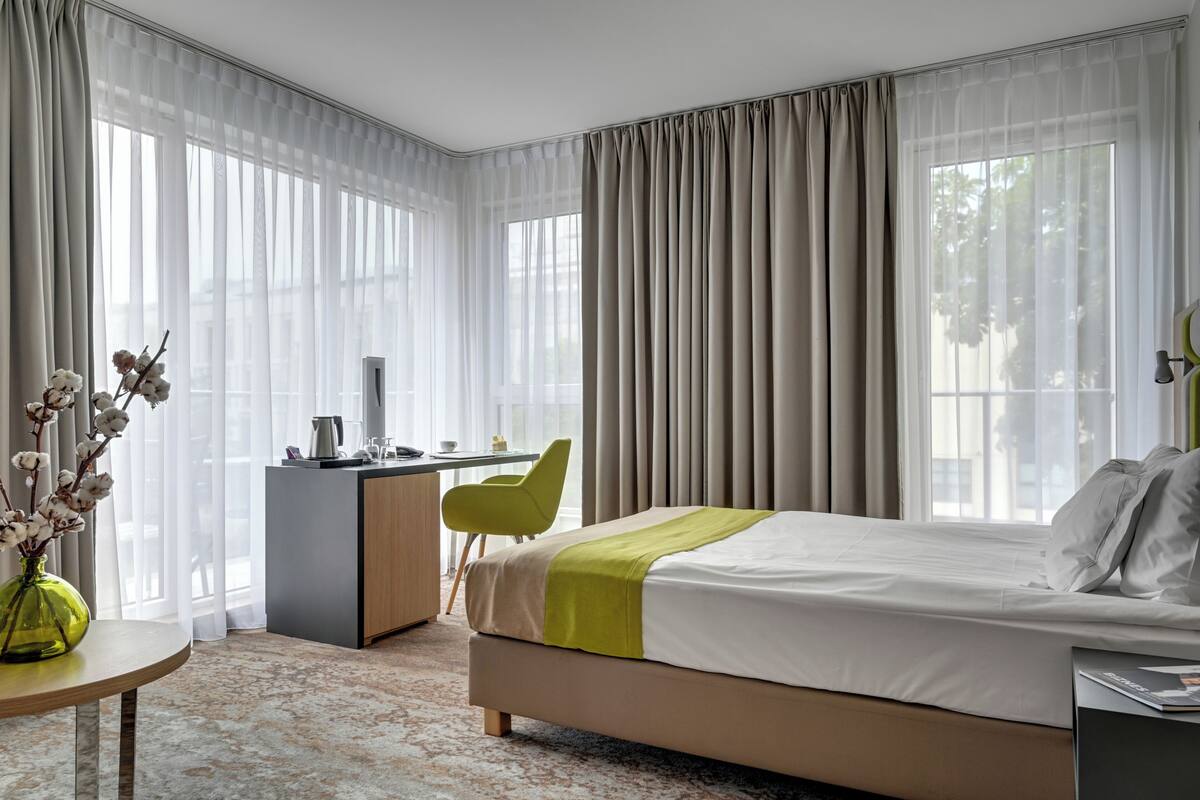 Quarto de hotel com cama, escrivaninha, cadeira e um vaso com flores.