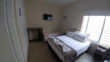 Quarto de hotel com cama, televisão, escrivaninha e janela.