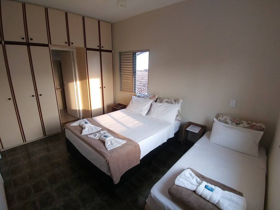 Um quarto com uma cama grande, uma cama menor, um guarda-roupa e uma janela.