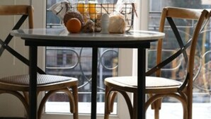 Uma sala de jantar com uma mesa e duas cadeiras, uma janela com vista para edifícios e piso de azulejos.