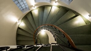 Uma escadaria em espiral com corrimão de madeira e uma claraboia acima.