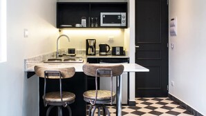 Cozinha compacta com micro-ondas, cafeteira e dois bancos.