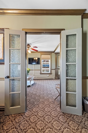 Quarto de hotel com piso carpetado, televisão, ventoinha no teto e janela com painéis de vidro jateado.