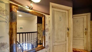 Um corredor com um espelho de madeira, uma escadaria e uma porta com placa de número.