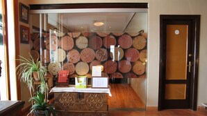 Uma receção com divisória de vidro, arte em parede com barris de madeira e uma porta com placa de identificação.