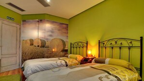 Quarto com duas camas, um mural de fardos de feno, parede verde e uma porta com a inscrição 'SALIDA'.
