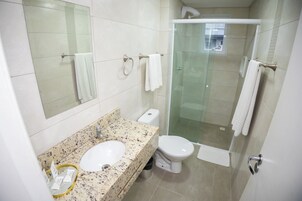 Casa de banho com bancada de granito, duas pias, sanita e cabine de duche com parede de vidro.