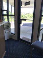 Entrada de hotel com carpete azul, balcão de recepção, uma cadeira e um aviso de 'Sem Quartos Disponíveis'.