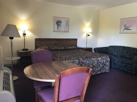Quarto de hotel com cama, sofá, mesa redonda e duas luminárias.