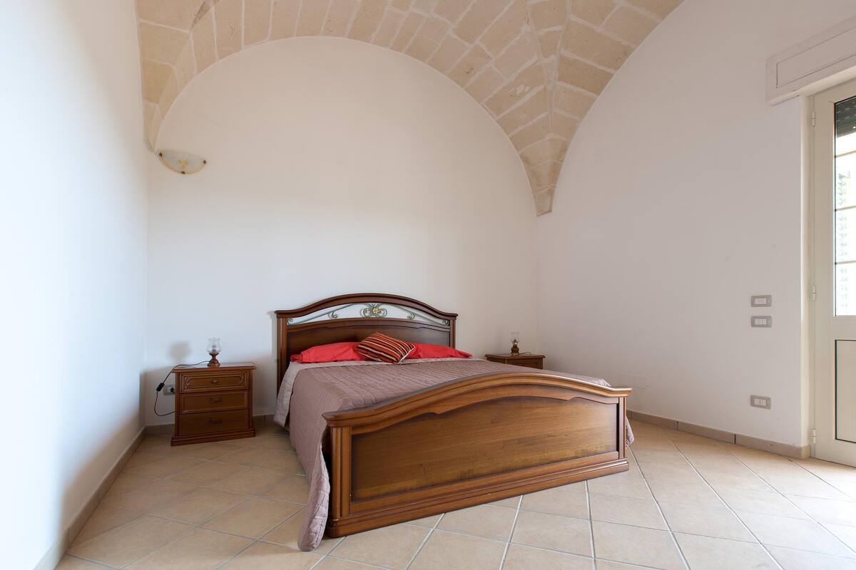 Quarto com cama de madeira, mesa de cabeceira e cômoda.