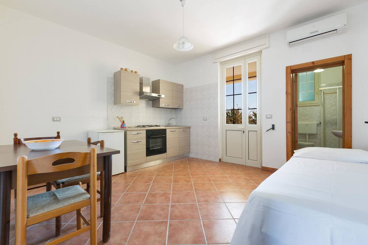 Cozinha compacta com mesa, cadeiras e uma cama em um quarto pequeno.