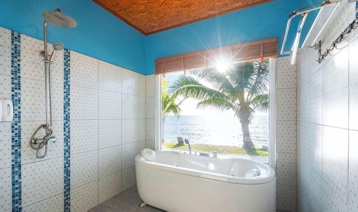Casa de banho com banheira, chuveiro e vista para o mar através de uma janela.