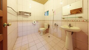 Casa de banho com azulejos brancos, sanita, lavatório e chuveiro.