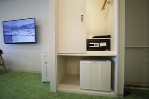 Quarto com televisão de tela plana presa na parede exibindo uma paisagem nevada, um armário branco com um dispositivo preto em cima e um eletrodoméstico pequeno branco no chão.