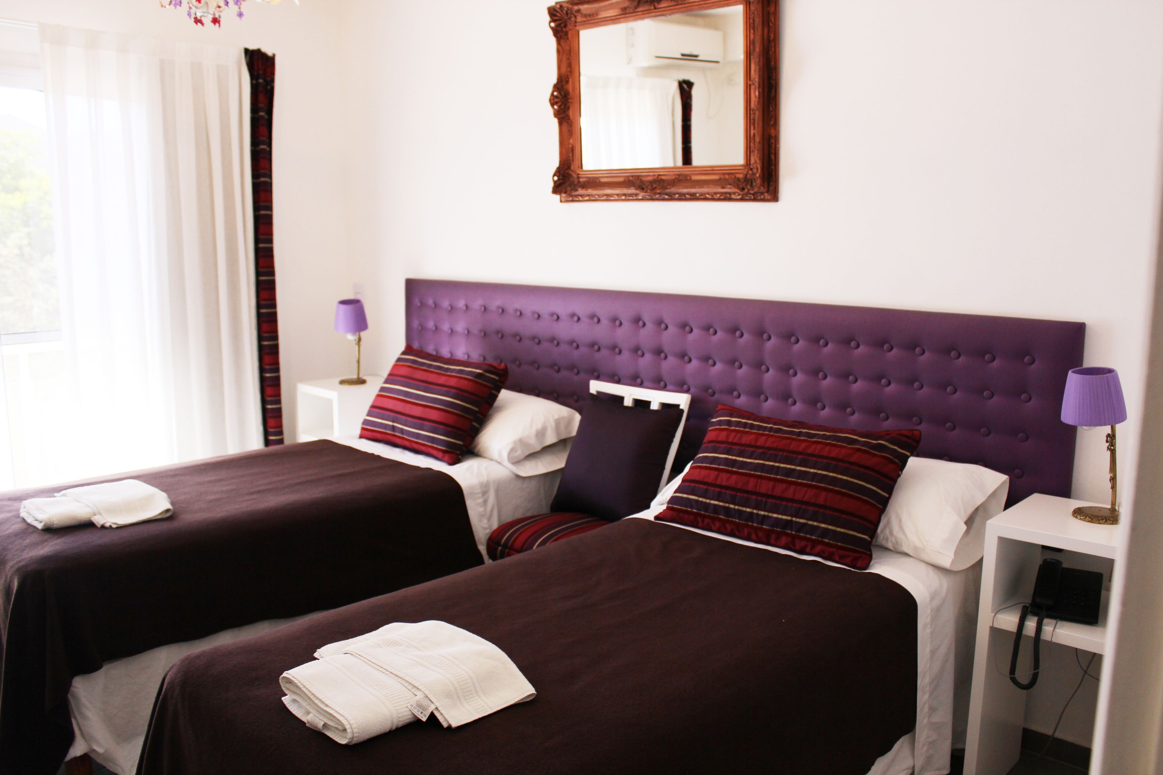 Quarto de hotel com duas camas, cabeceira roxa e espelho sobre as camas.