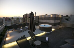 Terraço no telhado com espreguiçadeiras, banheira de hidromassagem e um guarda-sol.