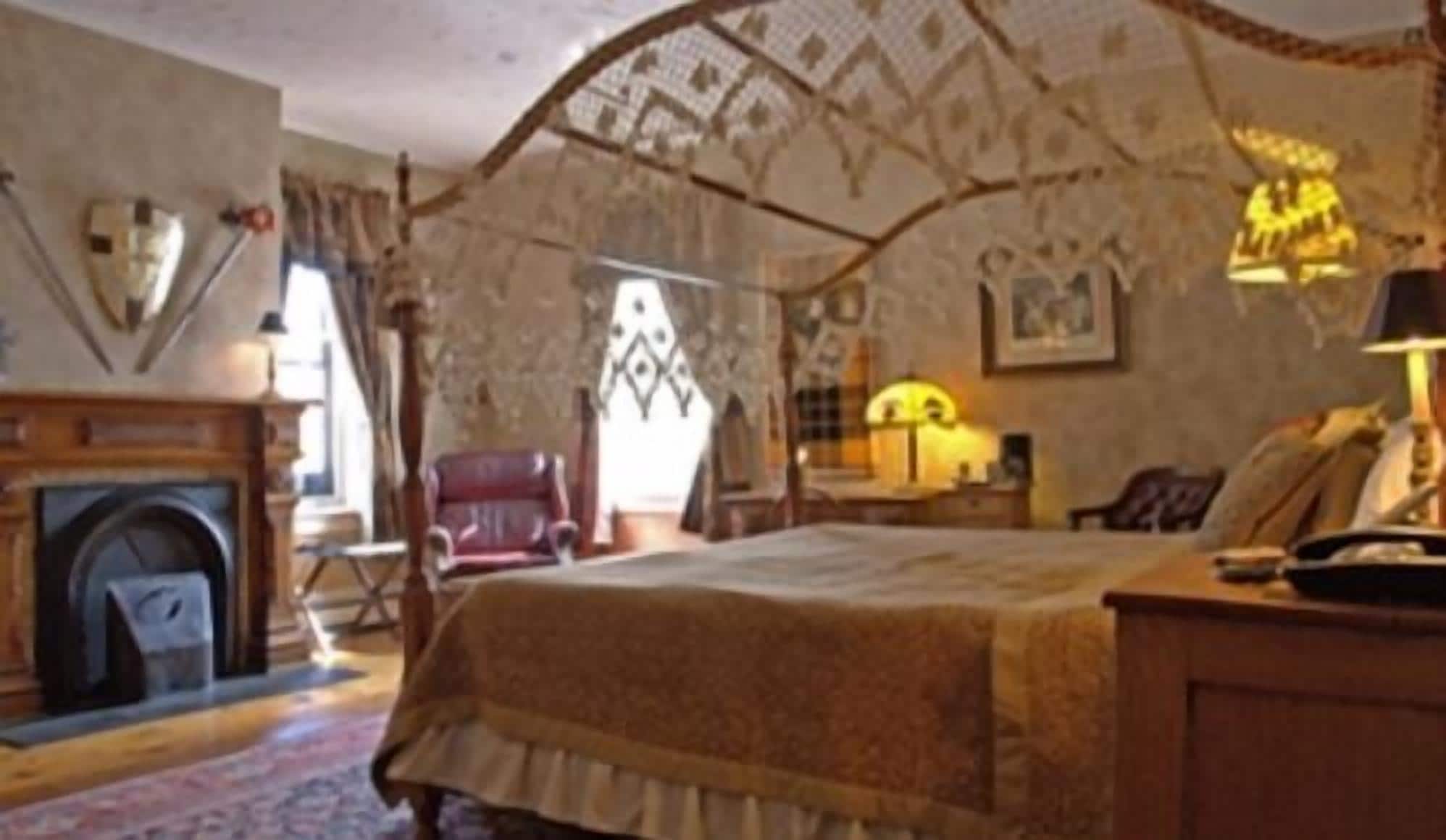 Um quarto com uma cama grande, lareira, uma cadeira e uma escrivaninha com abajur.