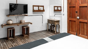 Quarto com cama, televisão, armário de madeira, espelho e porta de madeira.