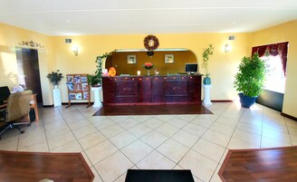 Uma área de recepção com um balcão de madeira, um relógio, quadros e um vaso com planta.