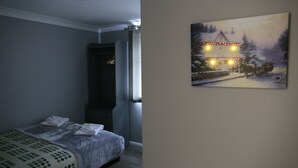 Quarto com cama, mesa de cabeceira e pintura de uma paisagem nevada iluminada na parede.
