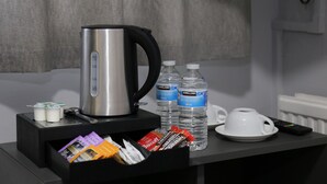 Quarto de hotel com máquina de café, duas garrafas de água, uma chávena e comando de televisão numa mesa.