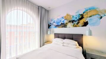Quarto de hotel com uma cama grande, um quadro na parede e vista para edifícios lá fora.