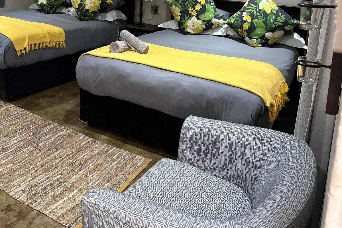 Quarto de hotel com duas camas, uma poltrona estampada, arte de parede decorativa de borboleta e uma luminária.