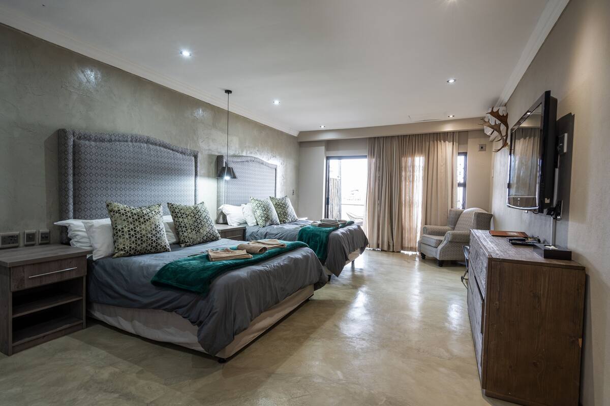 Quarto de hotel moderno com duas camas, uma escrivaninha, uma cadeira e um espelho grande.