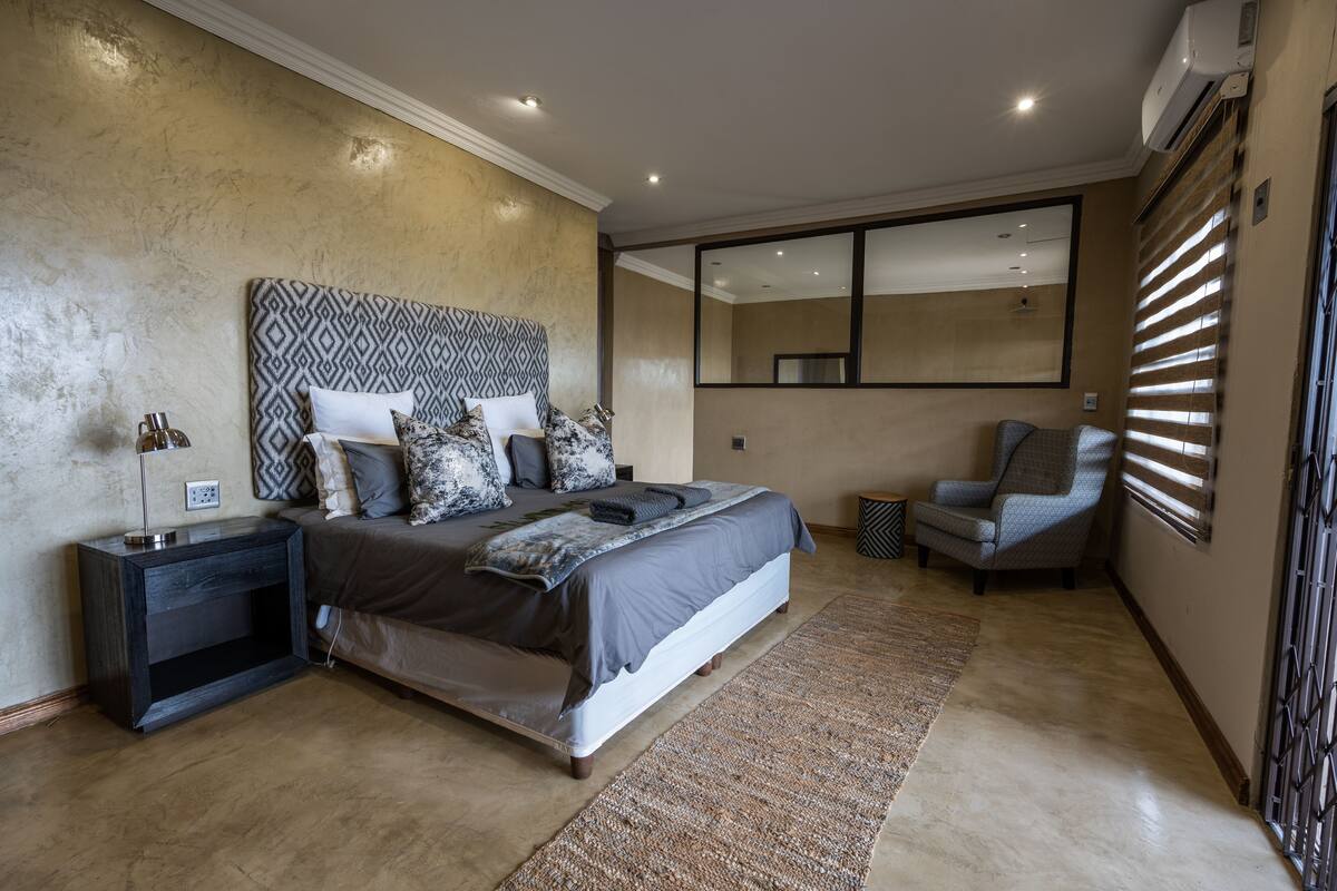 Um quarto moderno com uma cama grande, uma mesa de cabeceira, uma cadeira e um espelho amplo.