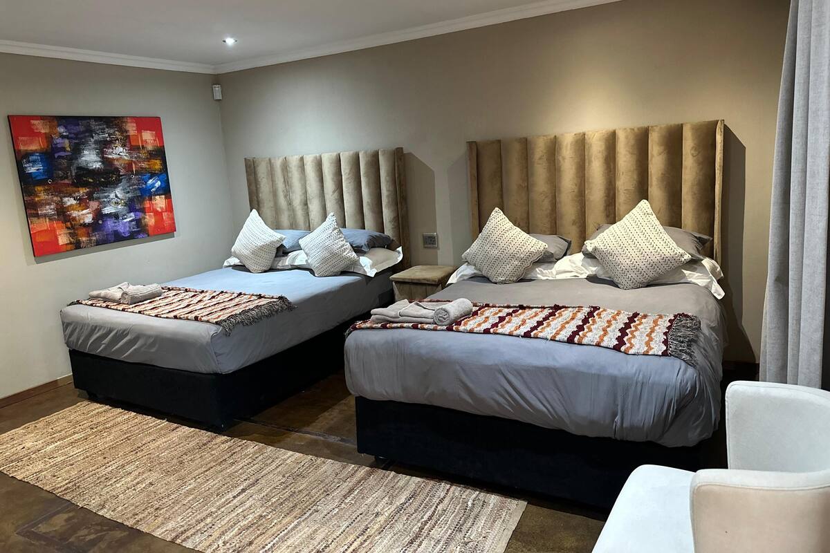 Quarto de hotel moderno com duas camas, uma pintura abstrata grande e um esquema de cores neutras.